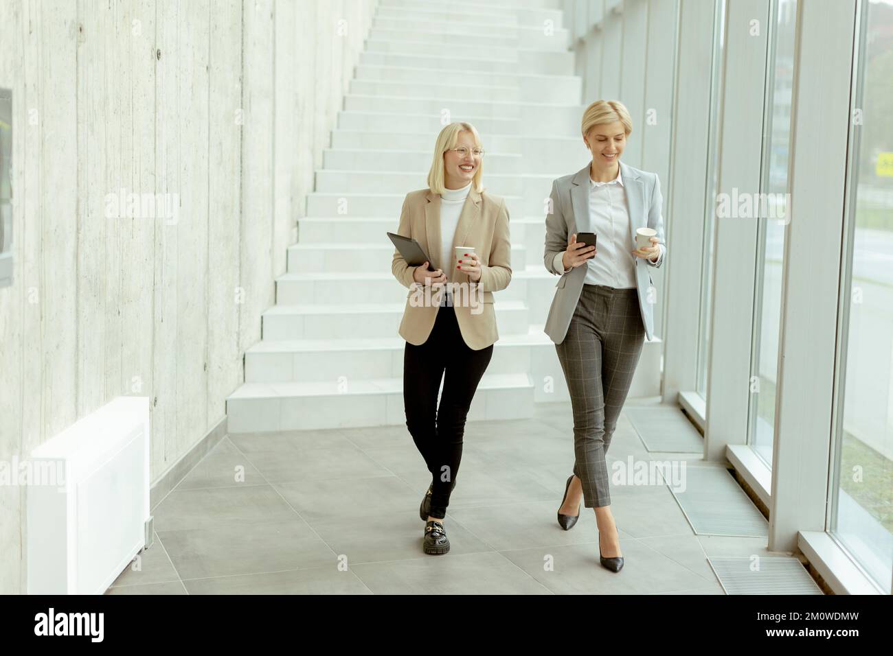 Two business women walking with digital tablet and mobile phone in the ...