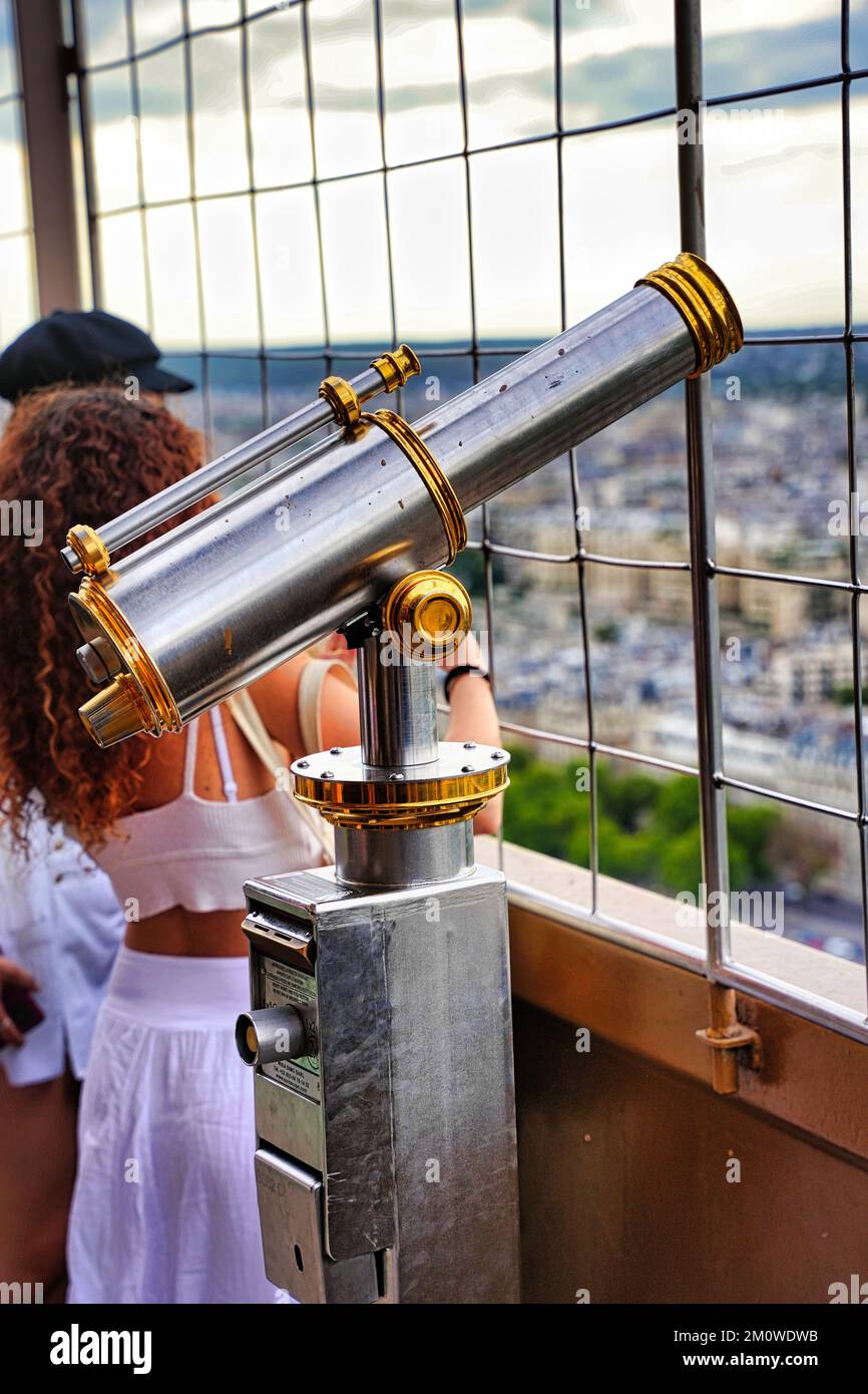 A vertical shot of a telescope behind metal bars with Paris city in the ...