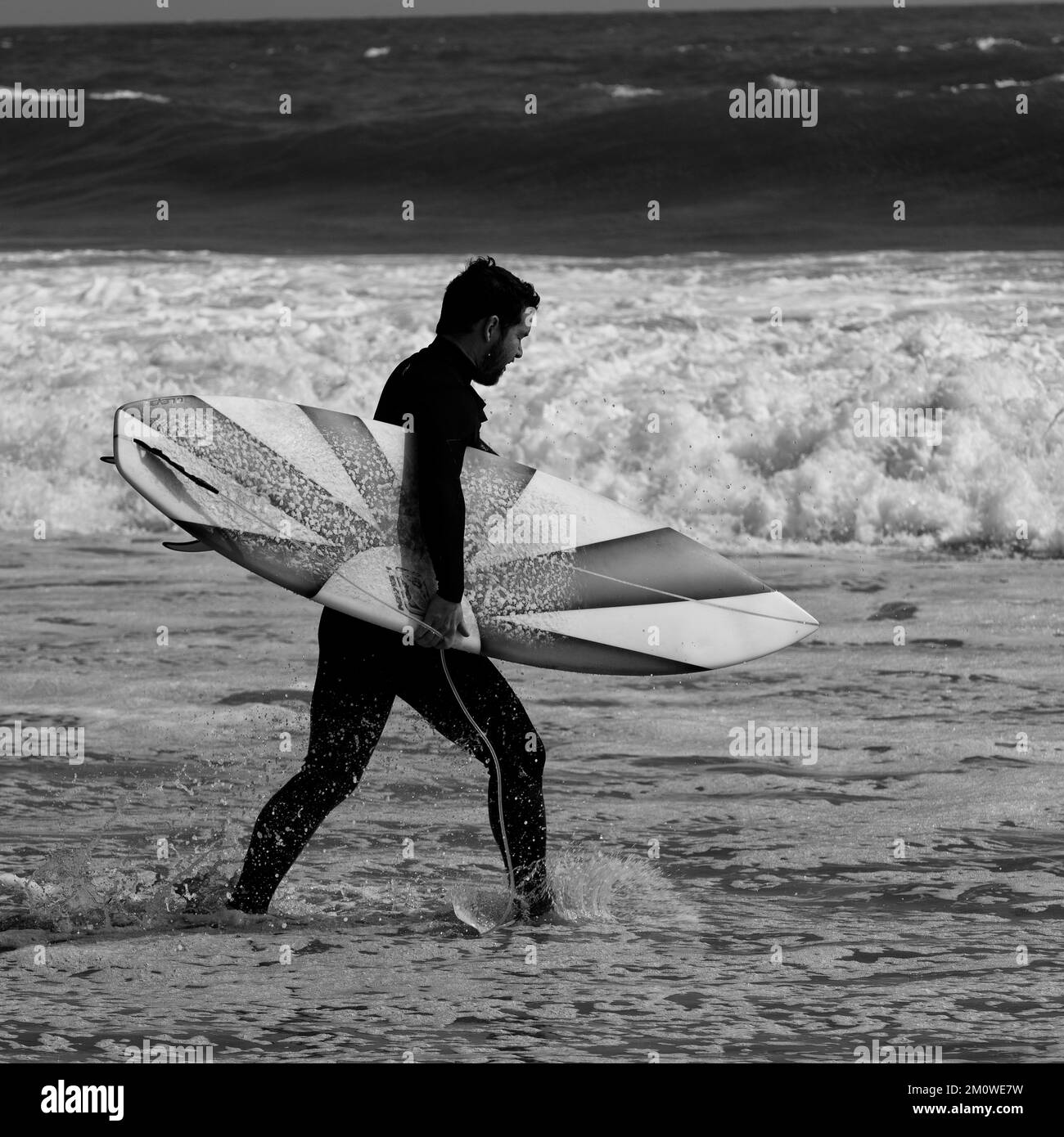 Surfier carrying his surfboard going out to surf - Black and white ...