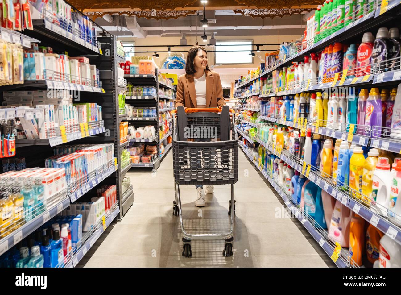 a woman with a cart walks between rows of shelves in a grocery store ...