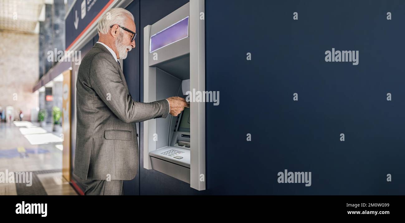 Profile view of senior entrepreneur using ATM machine. Elderly ...