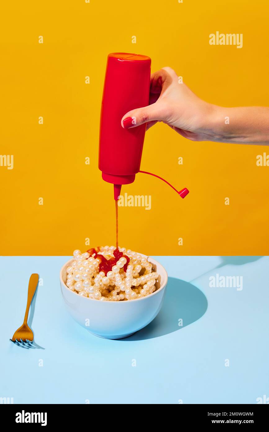 Female Hand Pouring Ketchup Into Bowl With Necklaces Symbolizing Pasta Noodles On Blue