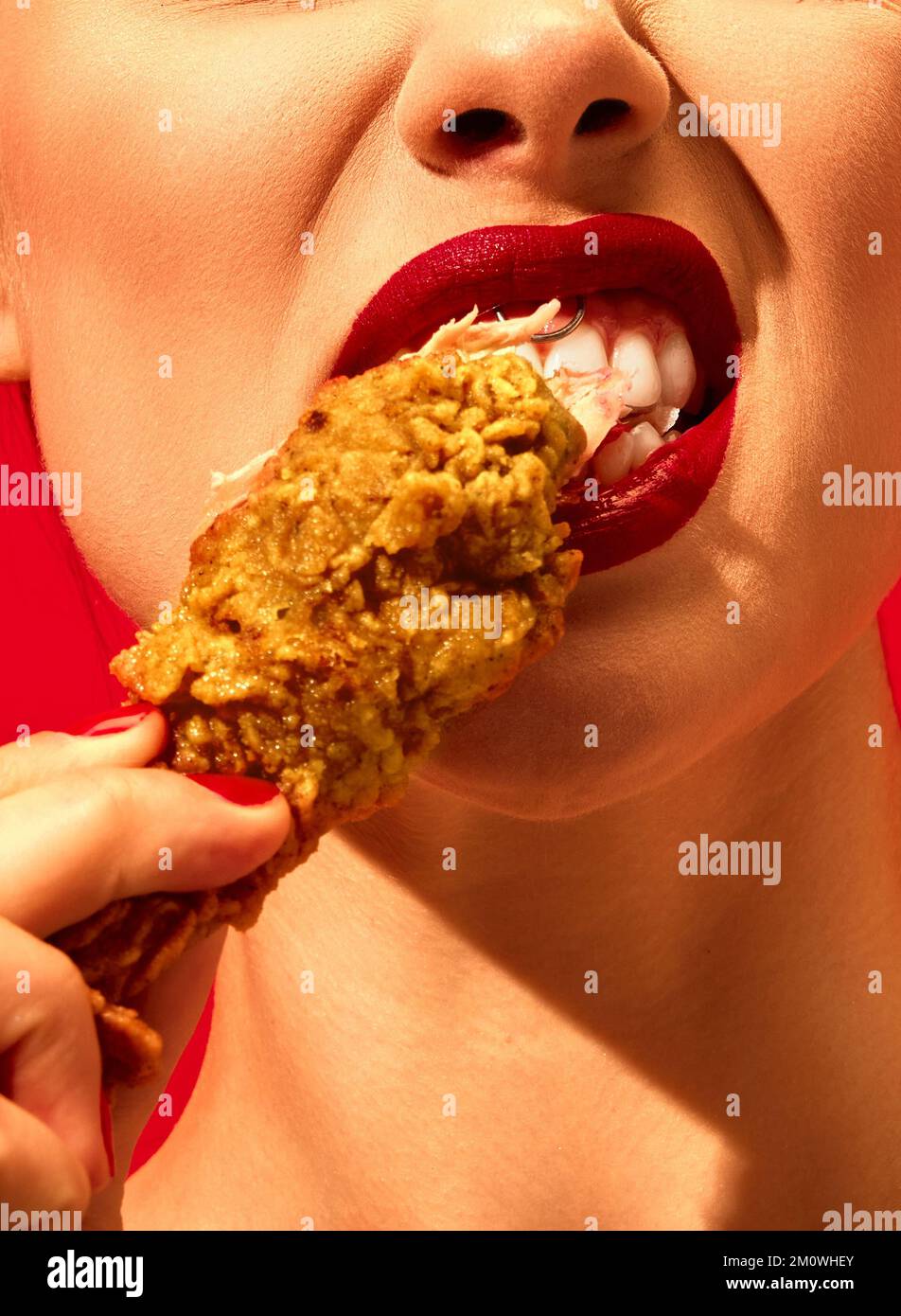 Close-up cropped image of young woman eating fried chicken, nuggets over vivid red background ...