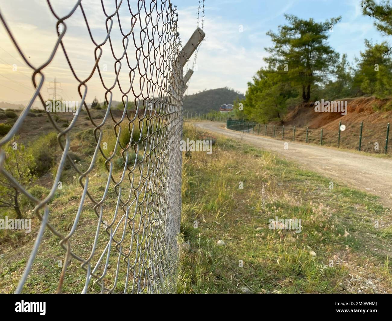 iron fence and barbed wire parallel to the dirt road. sunset in the ...