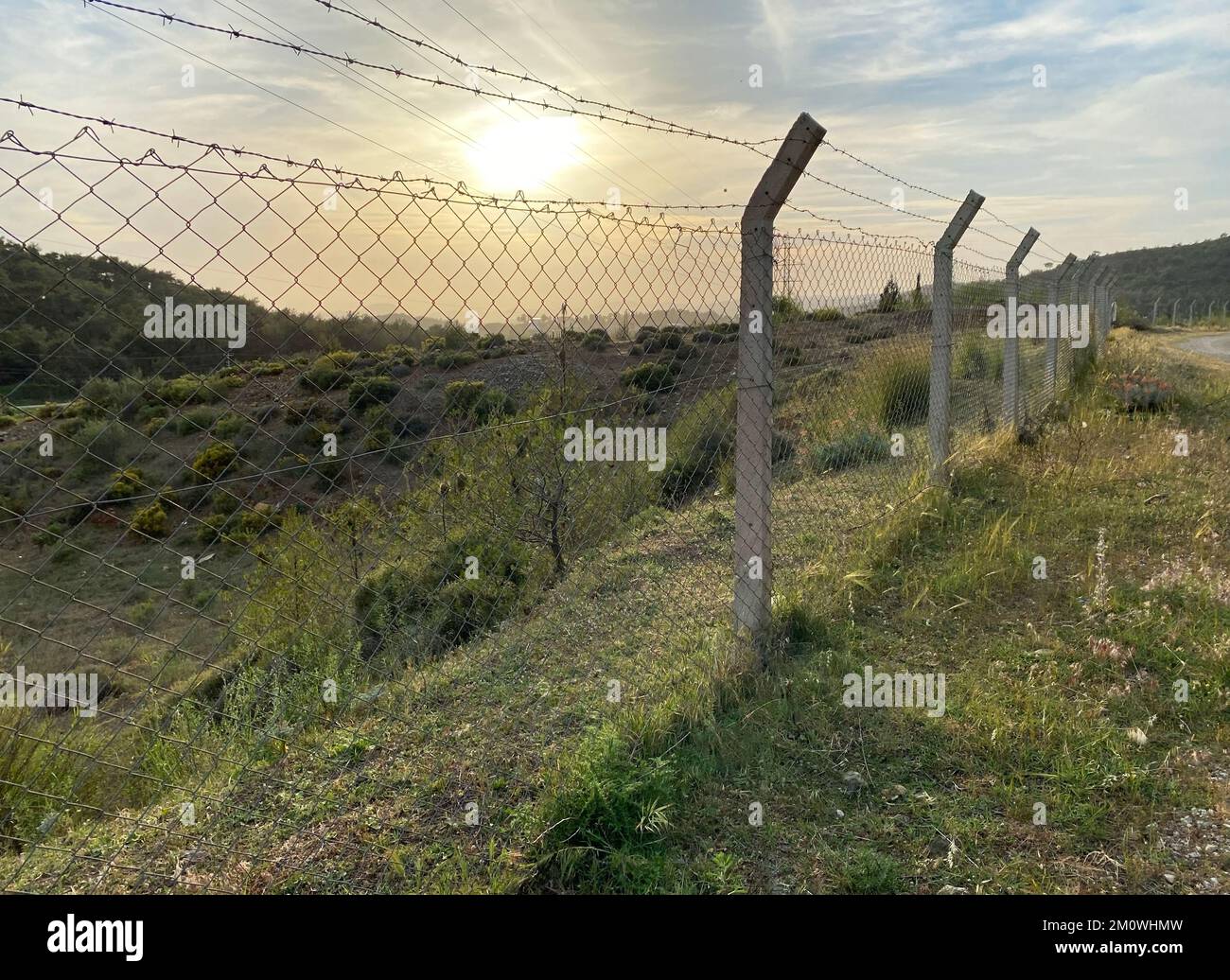 iron fence and barbed wire parallel to the dirt road. sunset in the ...