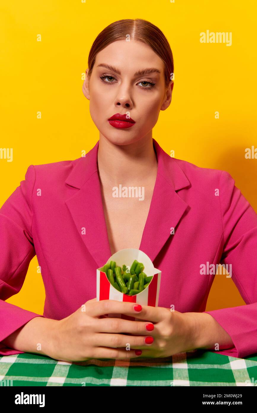 Emotionless, serious young woman in bright pink jacket holding green ...