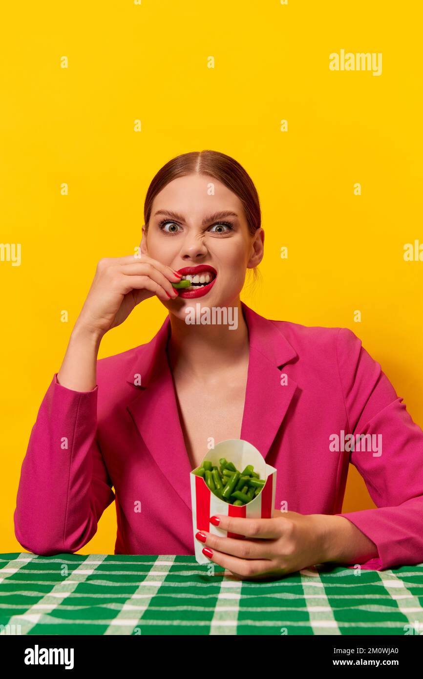 Emotional young woman in bright pink jacket eating green beans from ...