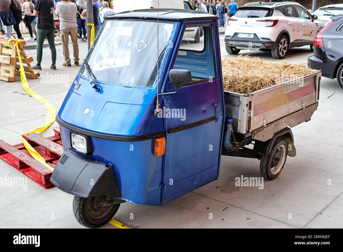A blue vintage Piaggio Ape tricycle with a sidecar fill with hay ...