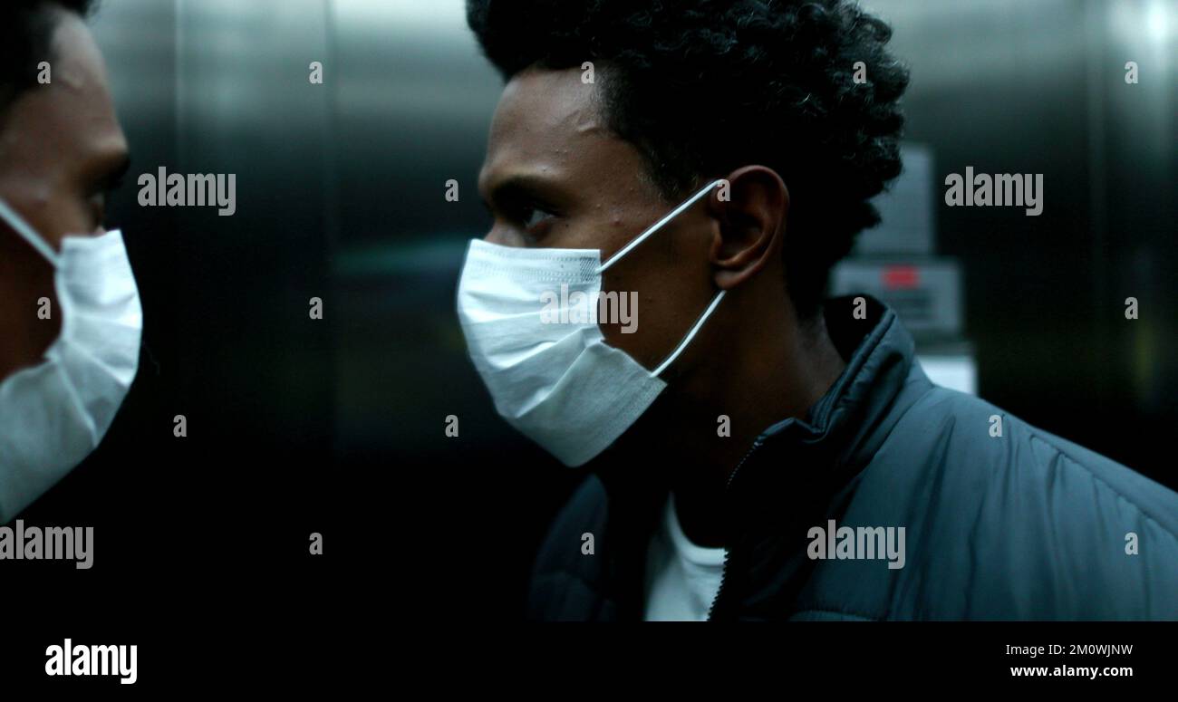 African american man putting on covid mask inside elevator, black ...