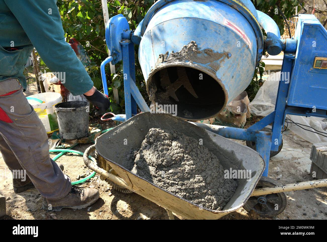 A bricklayer pours concrete from a temperer into a wheelbarrow ...