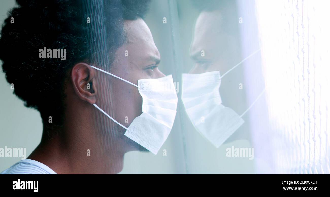 Black African man wearing virus mask looking out window, glass face ...