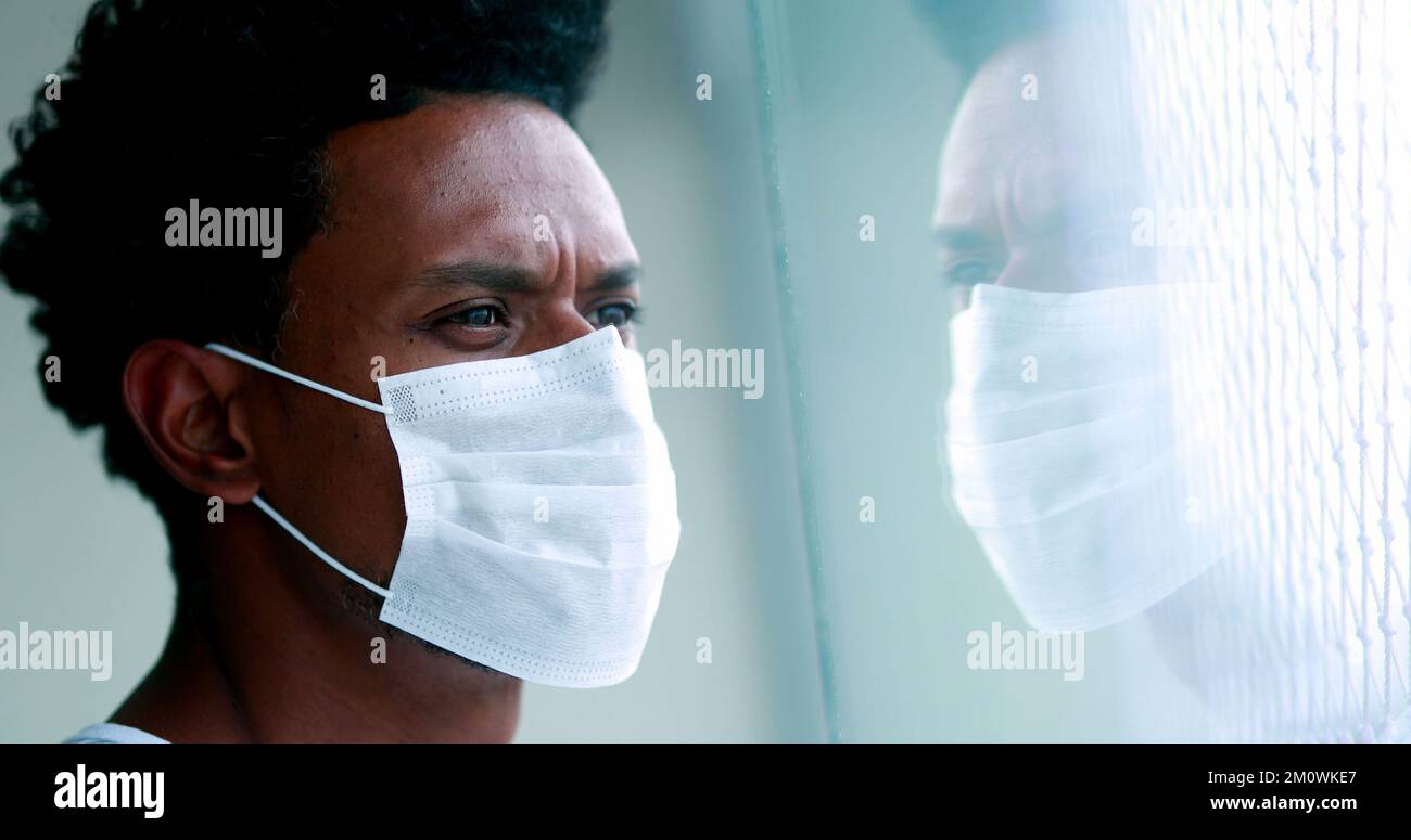 Black African man wearing virus mask looking out window, glass face ...
