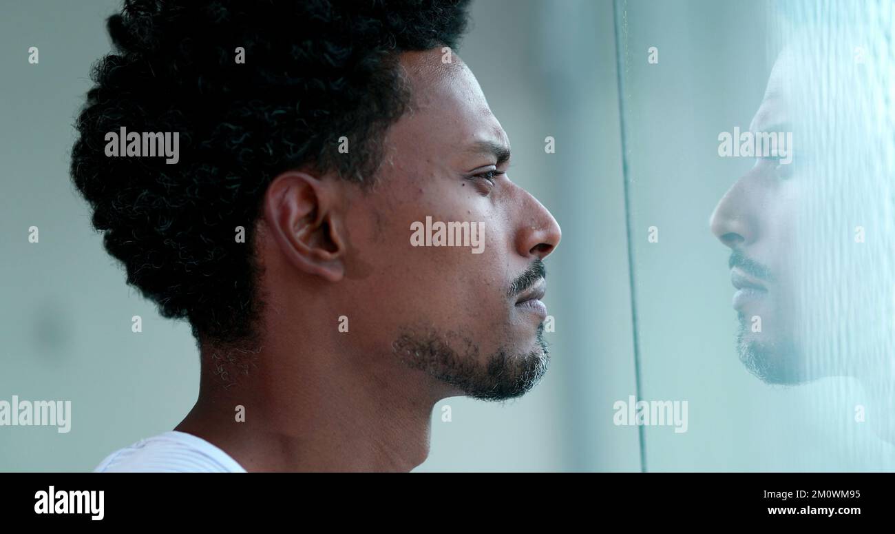Pensive African man looking out window indoors. Thoughtful black person ...