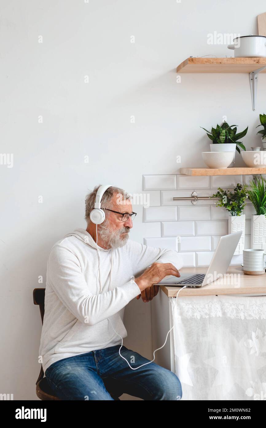 Handsome old man dressed in hoodie and eyeglasses is using laptop and ...
