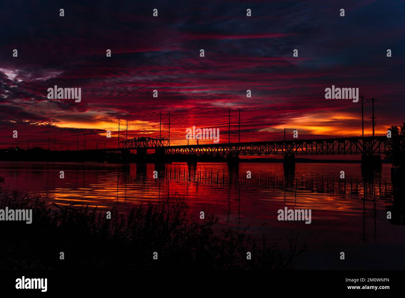 Scenic view of beautiful scarlet sunset sky with abstract clouds over bridge, undulating sea ...
