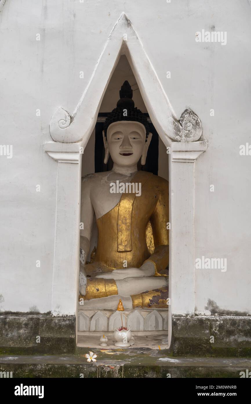 White and gold buddha statue sitting inside niche of ancient stupa at ...