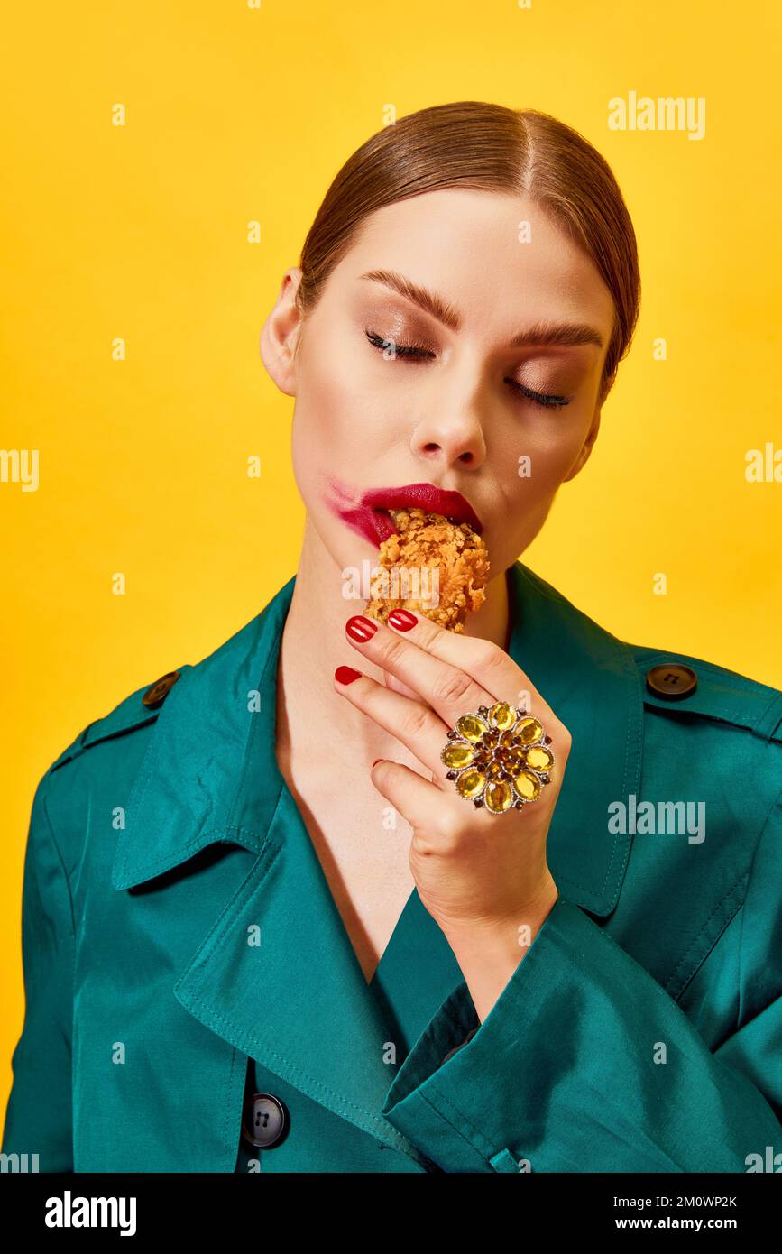 Young woman in green coat with red lipstick smudge, eating fried ...