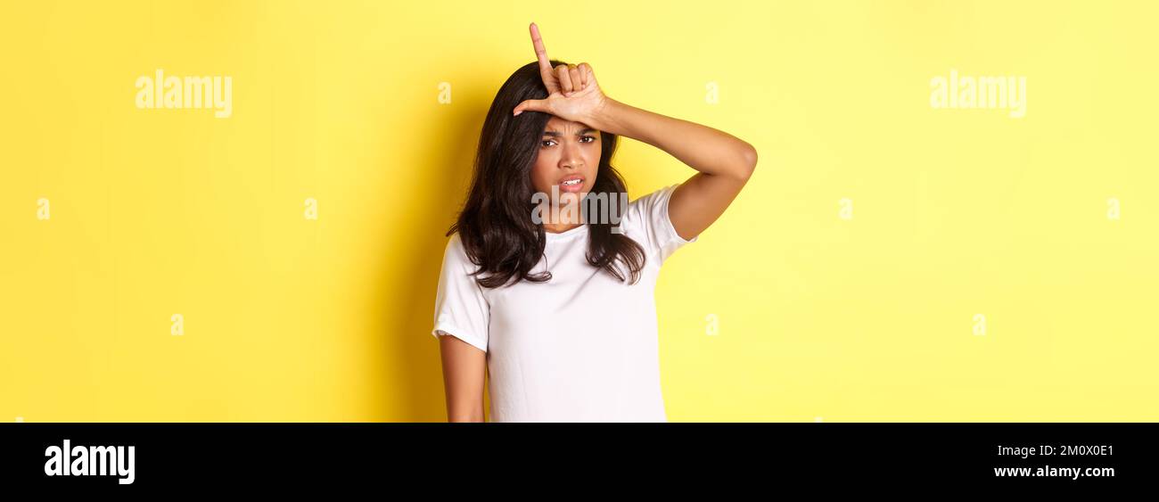 Image of sad african-american girl showing loser sign on forehead ...