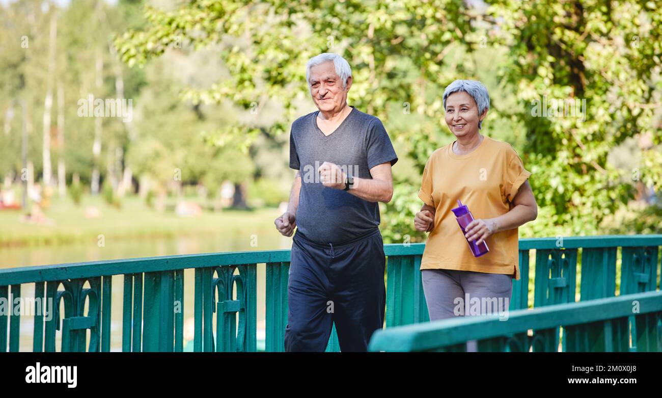 Asian and Caucasian senior wife and husband wear activewear strolling ...