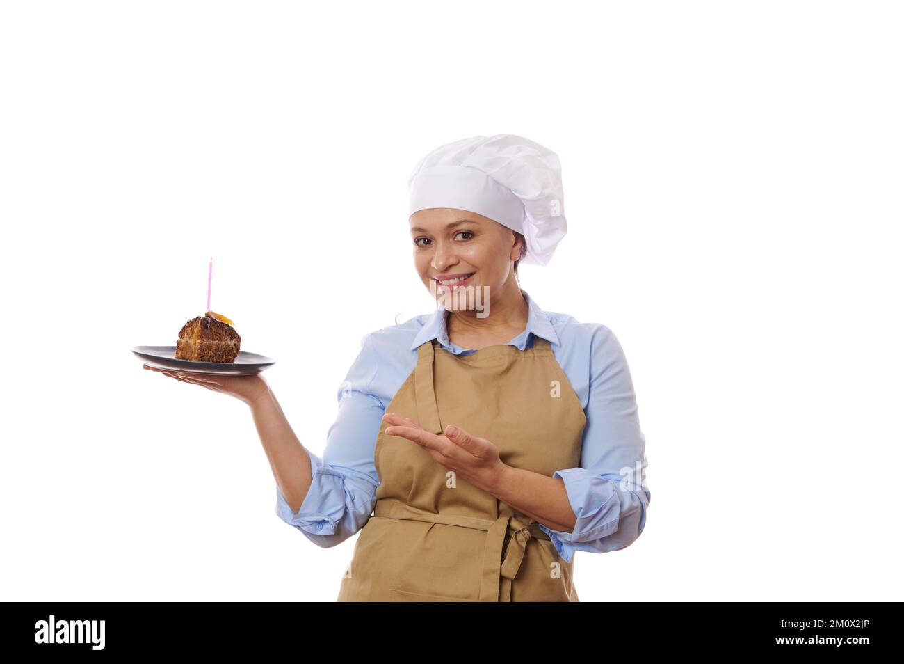 Charming positive woman baker in apron and hat, holds a piece of ...