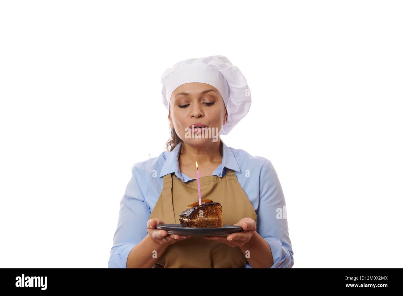 Female pastry baker, chef confectioner in beige apron and hat, blows ...
