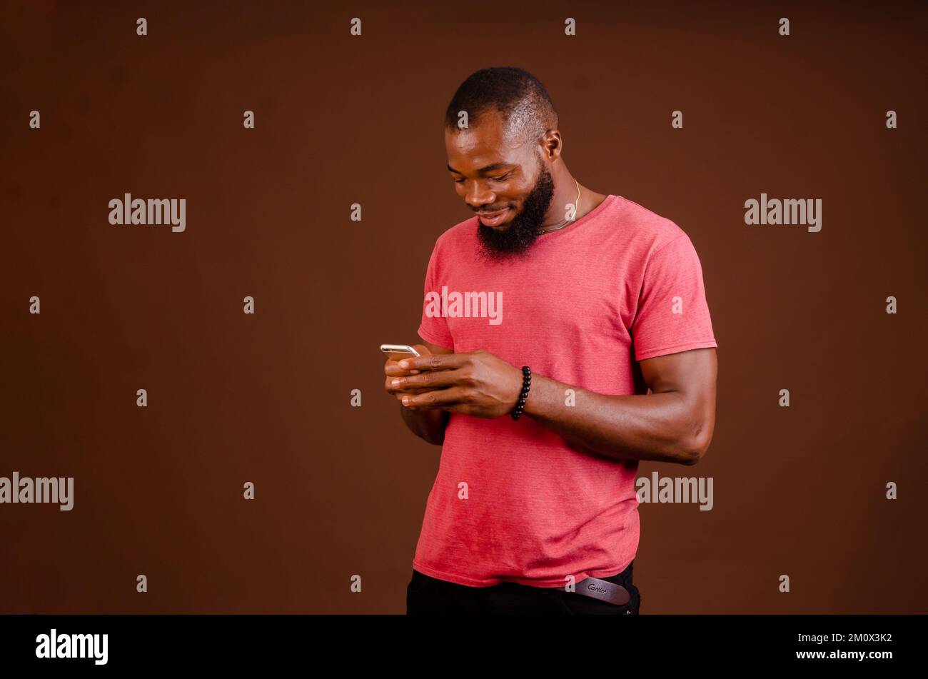 An attractive happy African man scrolling his phone isolated on a brown ...