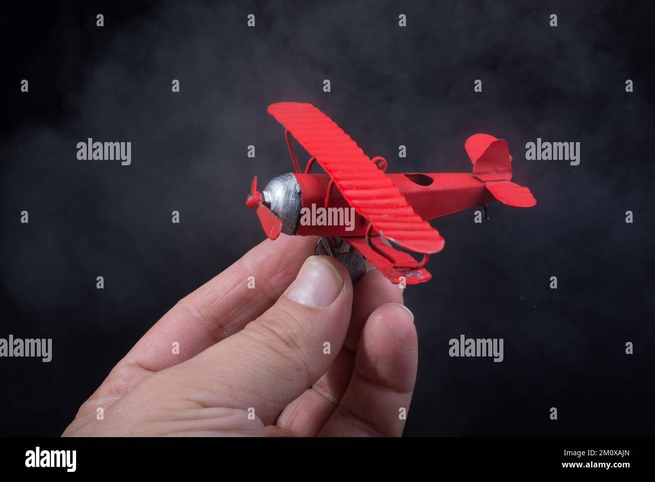 Hand holding a red toy plane on a black background Stock Photo - Alamy