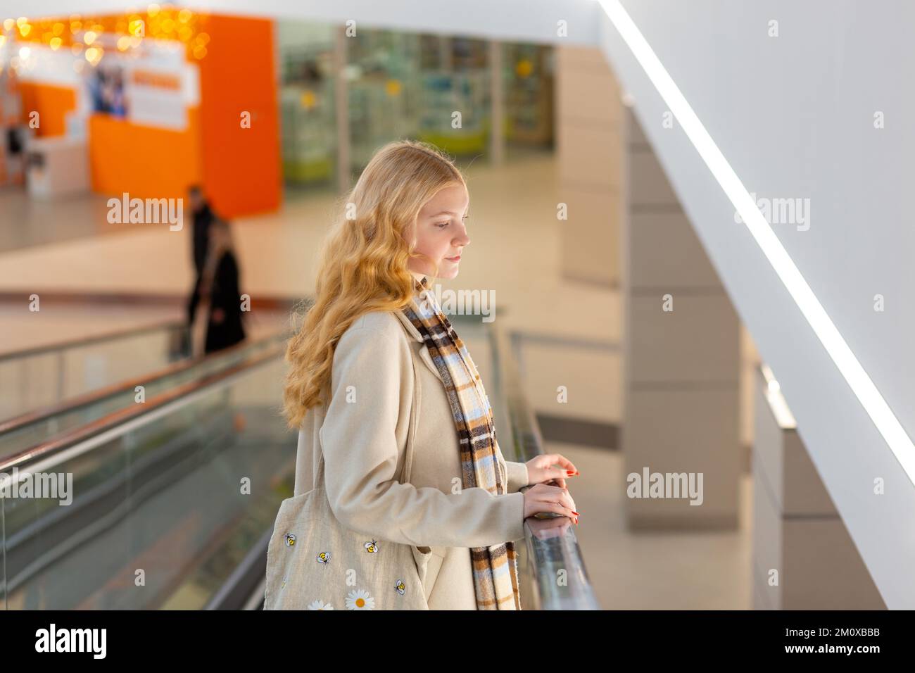 Young woman with long blond hair moving up on escalator at shopping ...