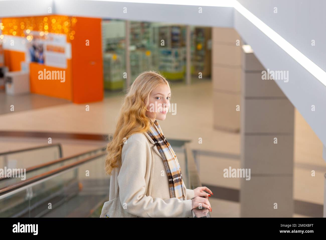 Young woman with long blond hair moving up on escalator at shopping ...