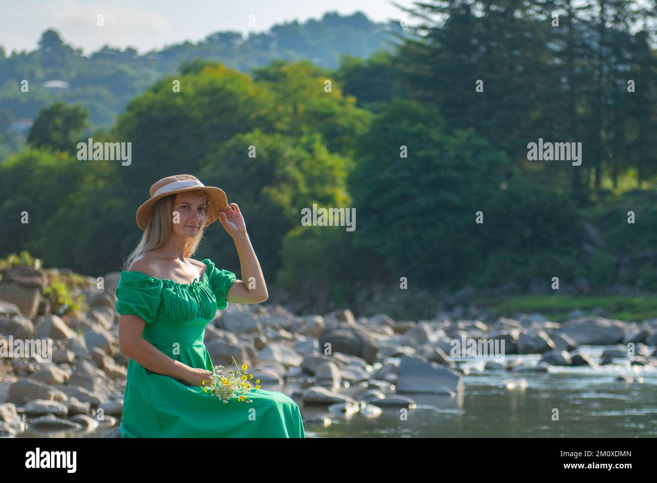 a girl in a hat is sitting on the rocks by the river Stock Photo - Alamy