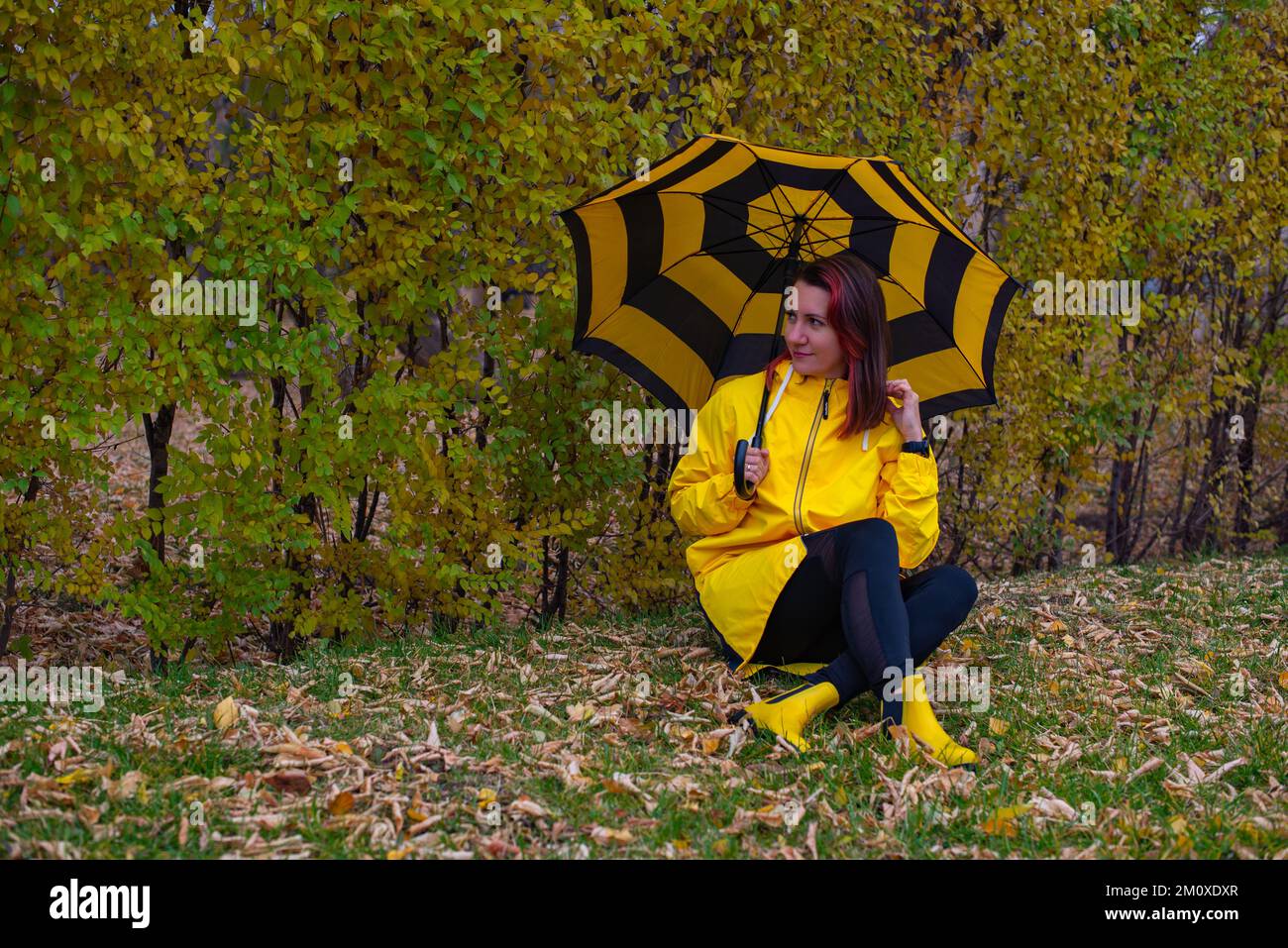 a thoughtful girl is sitting on the lawn in a yellow raincoat Stock ...