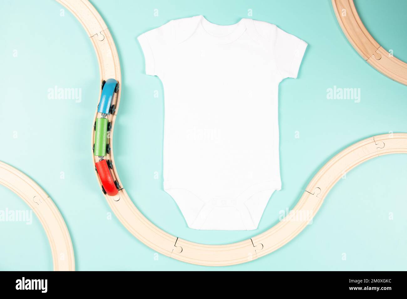 White cotton baby short sleeve bodysuit and wooden toy train on light ...