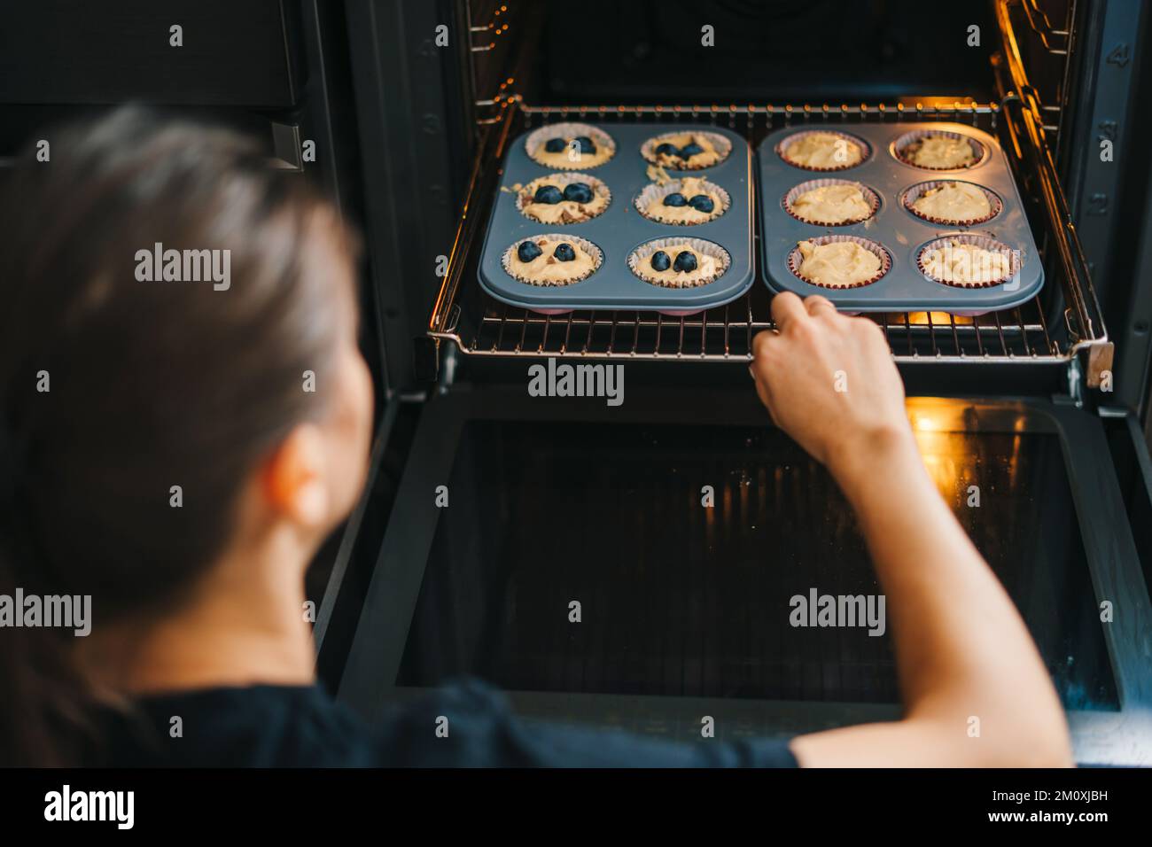 Woman's hands putting uncooked muffins with blueberries to oven in ...