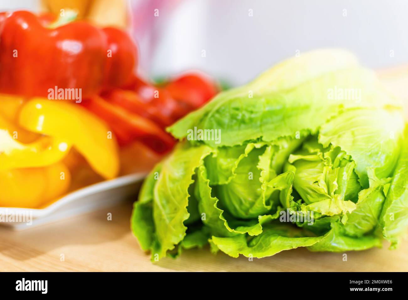 A closeup shot of a head of lettuce near sliced bell peppers on a ...