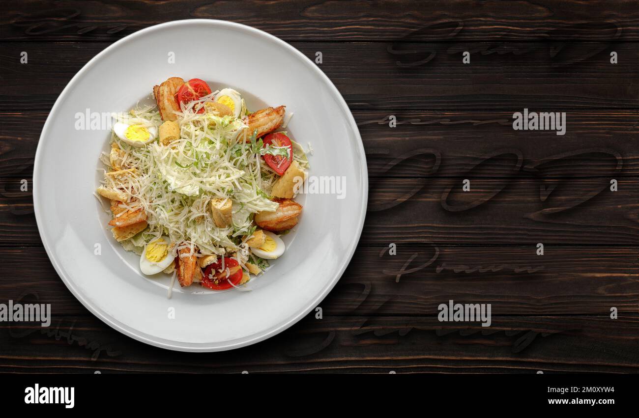 Caesar salad with shrimps, on a plate, on a dark background. With place ...
