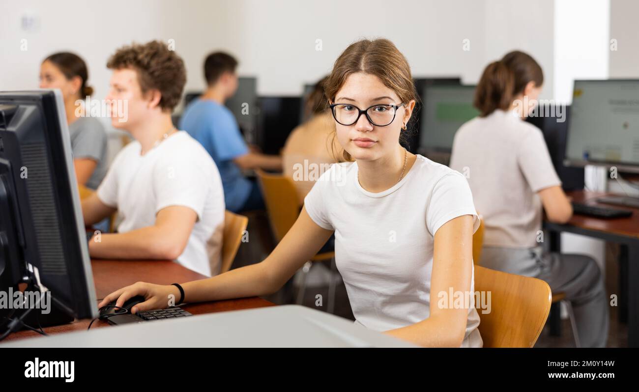 Positive female teenager in glasses learning computer science while she ...
