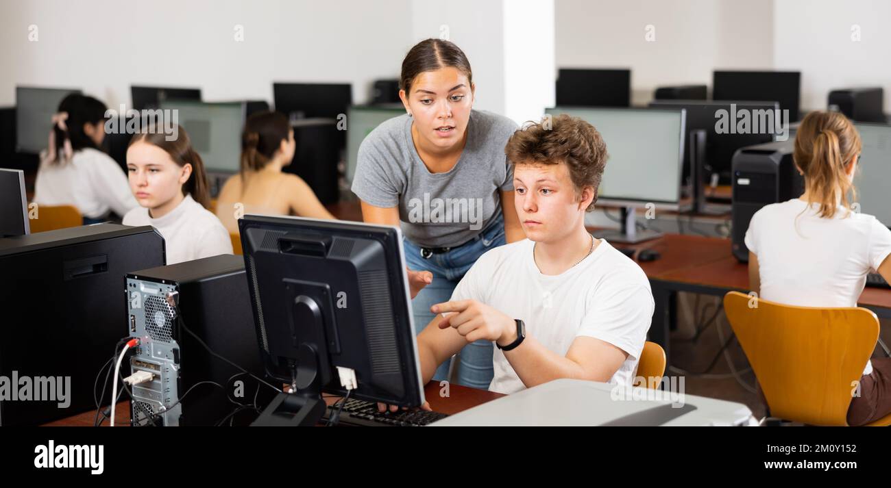 Young woman teacher helping concentrated teen male student with his ...