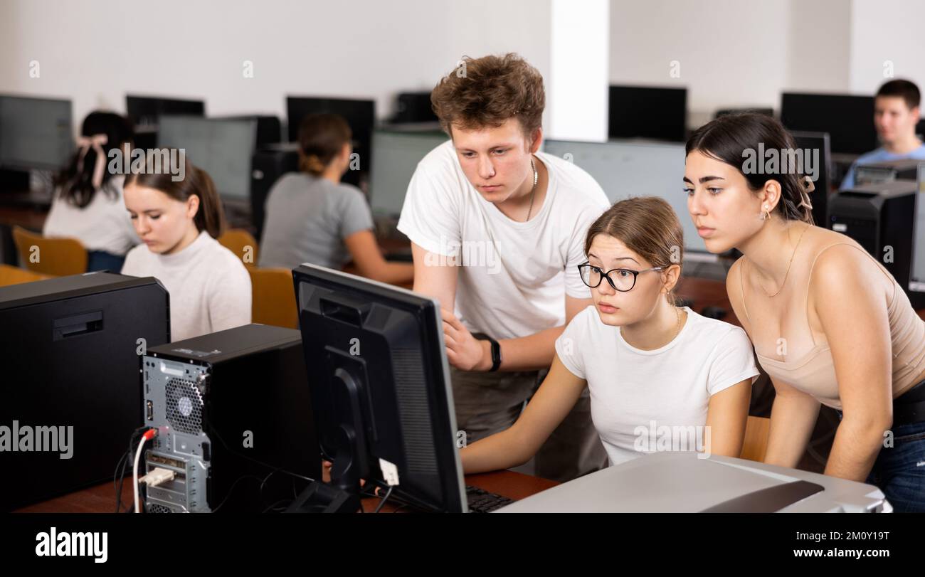 Concentrated boy helping young female students working with pc in ...