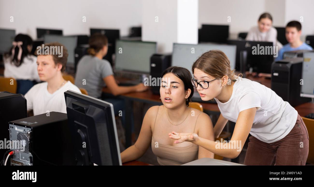 Teenager girl helps girlfriend solve problem on computer in school ...