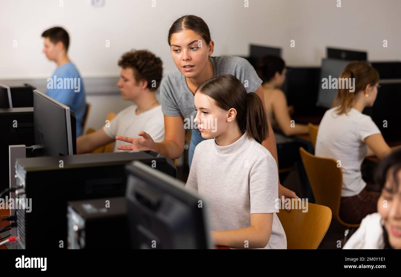 Young female teacher working with schoolgirl in computer class of ...