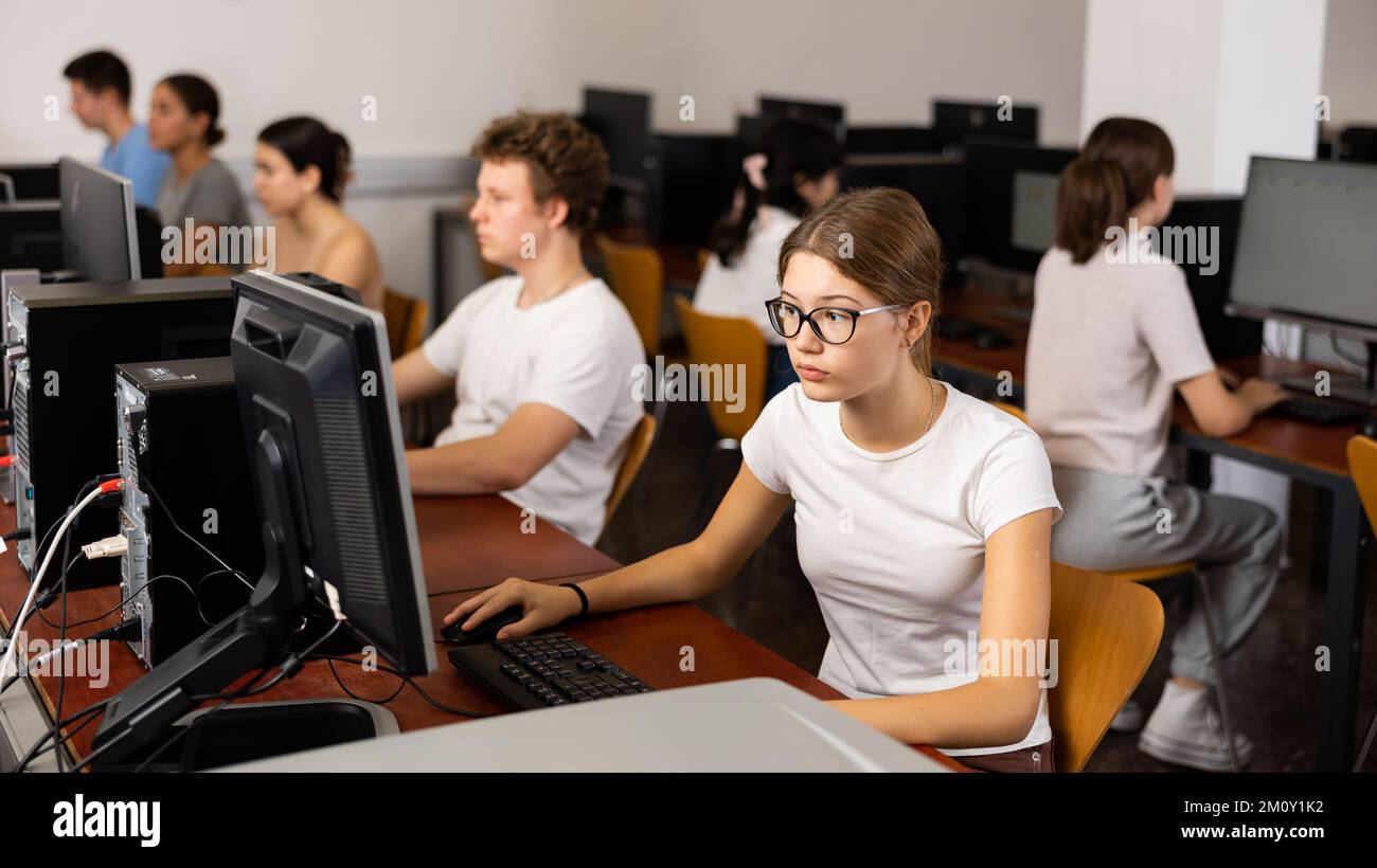 Clever female teenager wearing glasses and solving tasks of computer ...