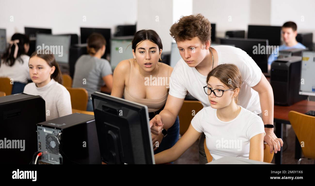 Clever teenagers helping to the female classmate while she is learning computer science in the ...