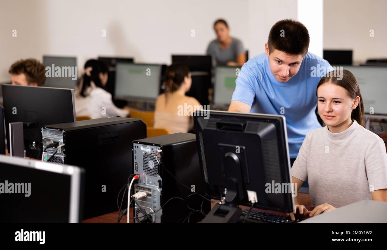 Smart teen schoolboy helping cute girl classmate sitting at computer ...