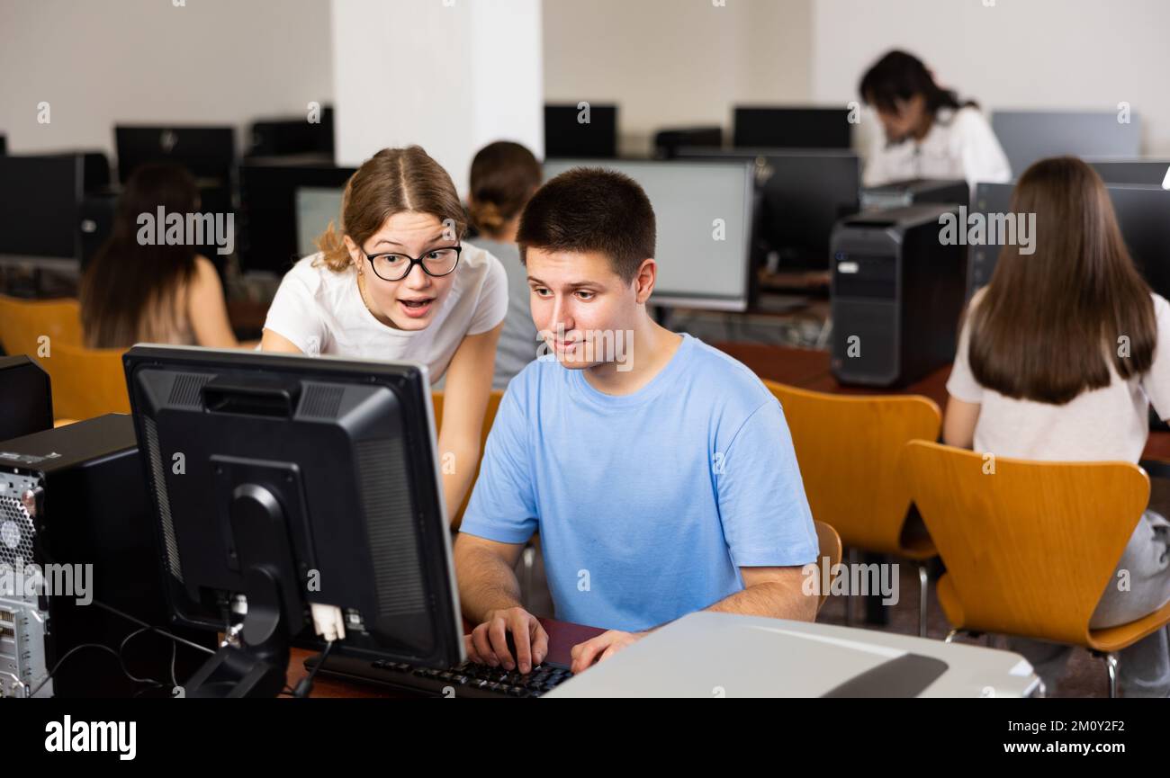 Teenager girl helps friend solve problem on computer in school class ...