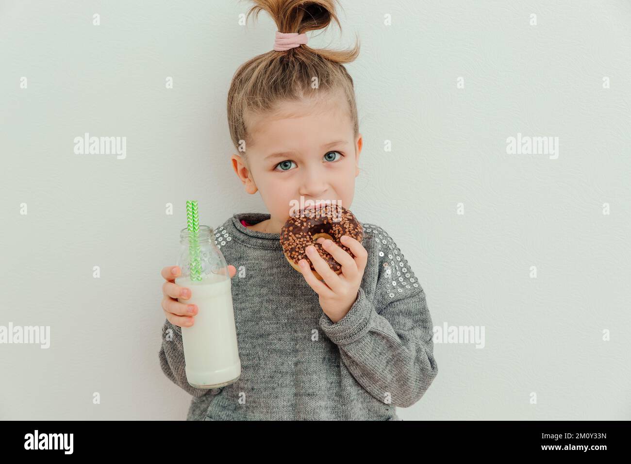 Lovely little girl is eating chocolate donut with bottle of milk ...