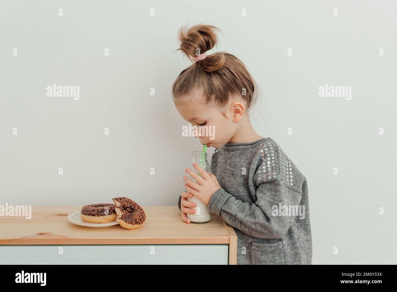 Lovely little girl is eating chocolate donut with bottle of milk ...