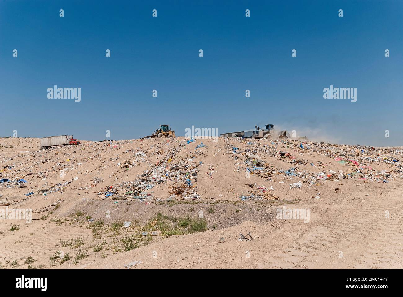 A soil compactor bulldozer kicks up a dust cloud at the top of a hill ...