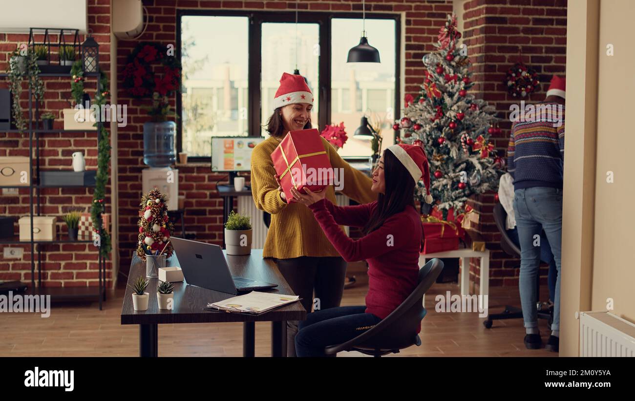 Colleagues giving presents to celebrate christmas eve at work, celebrating winter holiday in ...