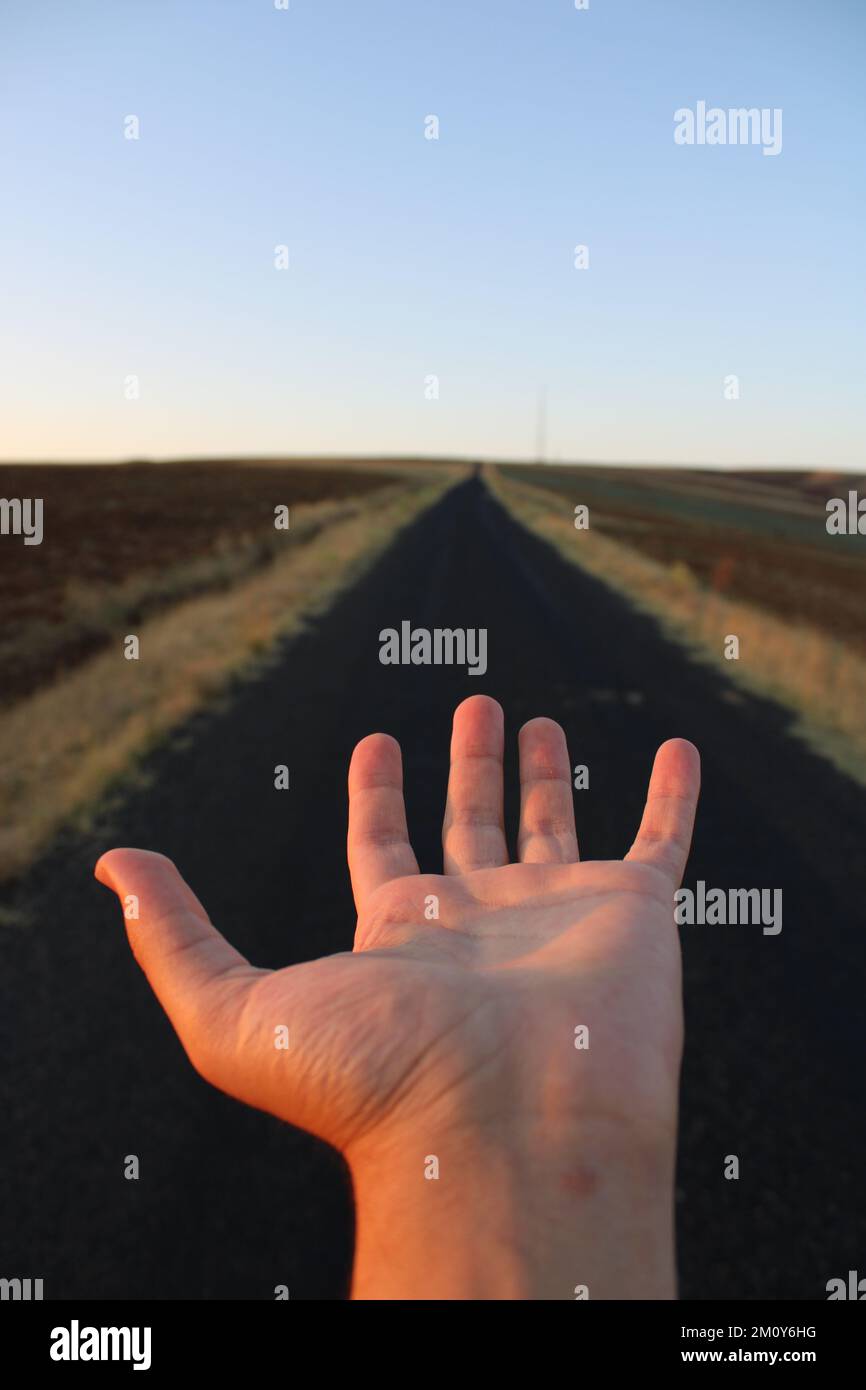 A thin road with long paths between fields. hand of a man. Asking for ...