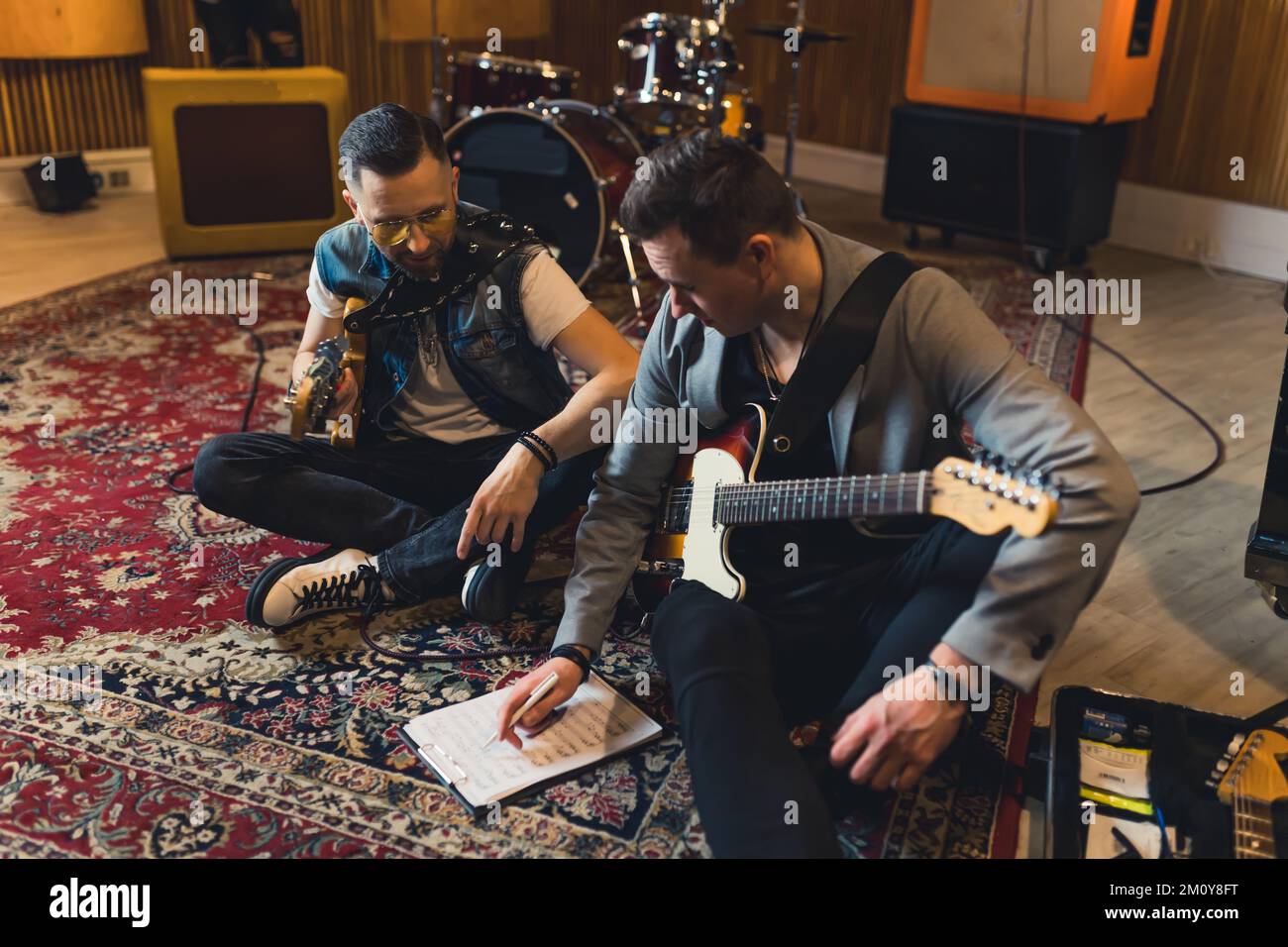 Male guitarists of a music band learning a new song, sitting on the ...